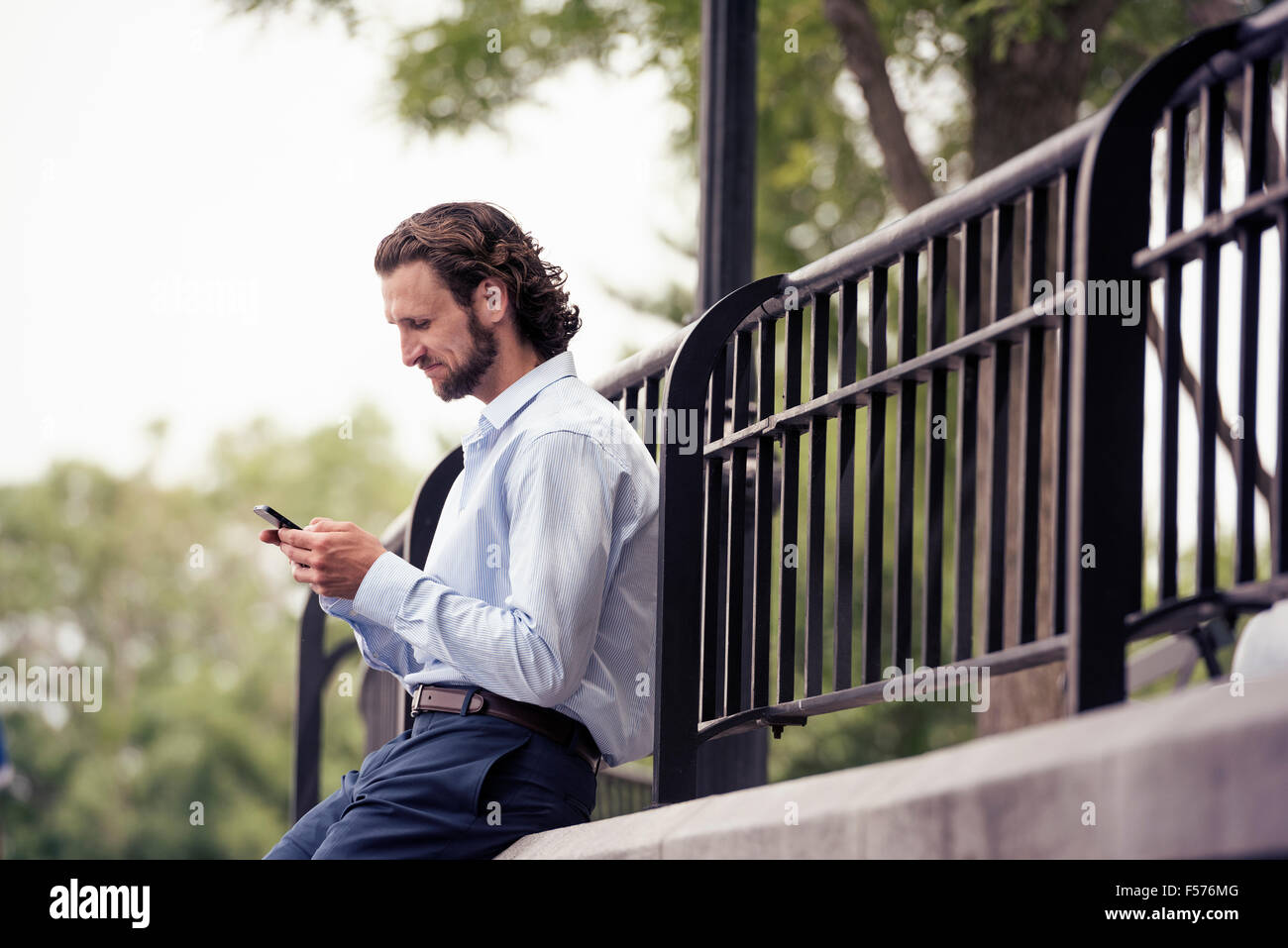 A man pausing on the street, sitting on a step checking his cell phone ...