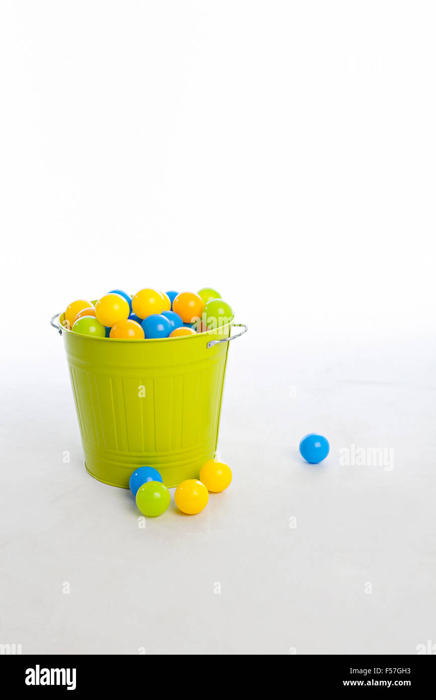 a green metal bucket full of plastic multi-colored balls on a white ...