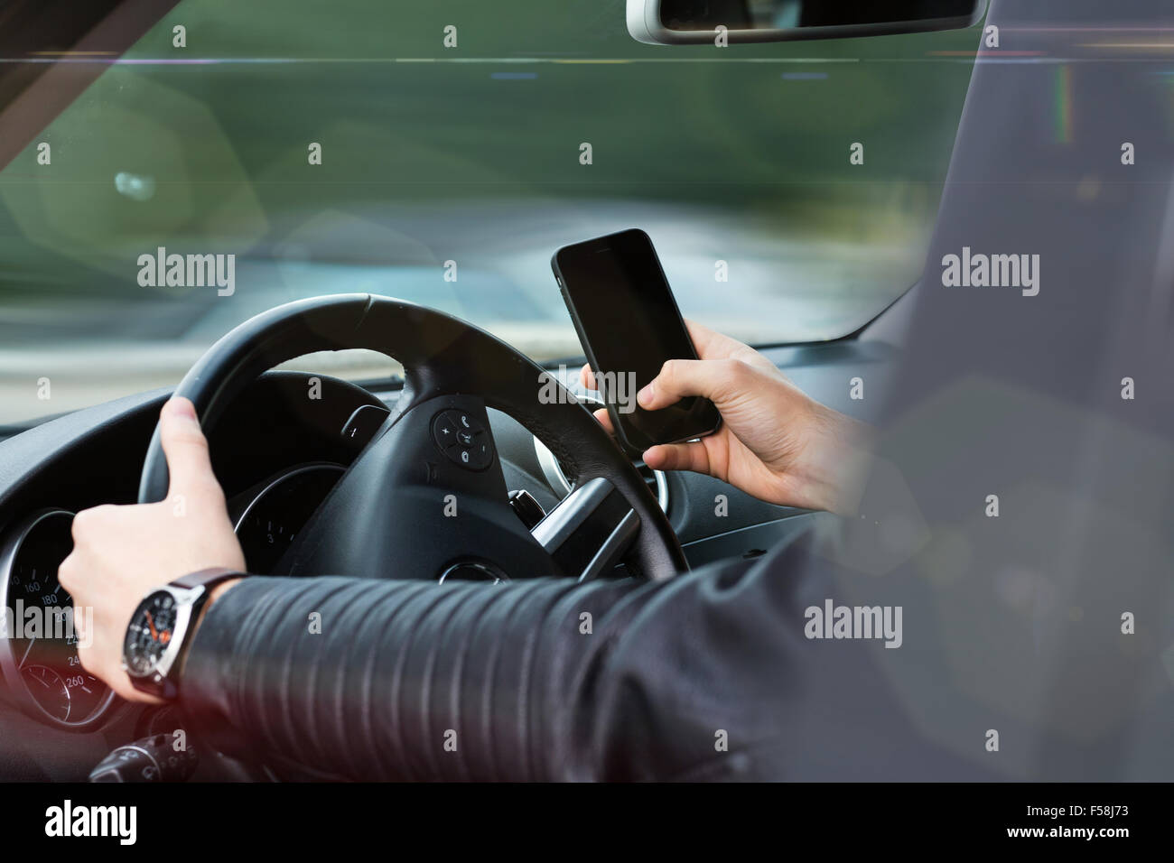 The hands of a young man driving and using a cell phone simultaneously ...