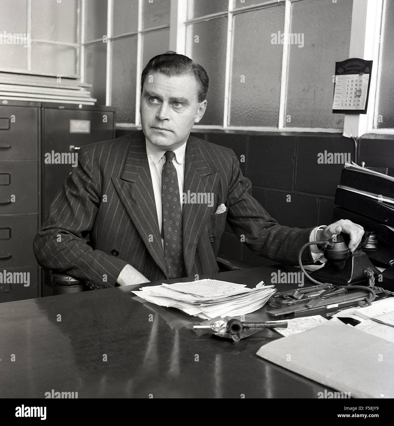 1950s historical, company manager in office with paperwork and pipe on ...
