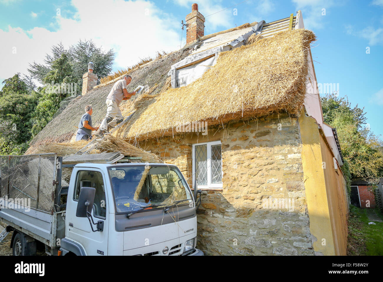 Skilled thatchers at work restoring a thatched roof on a cottage in ...