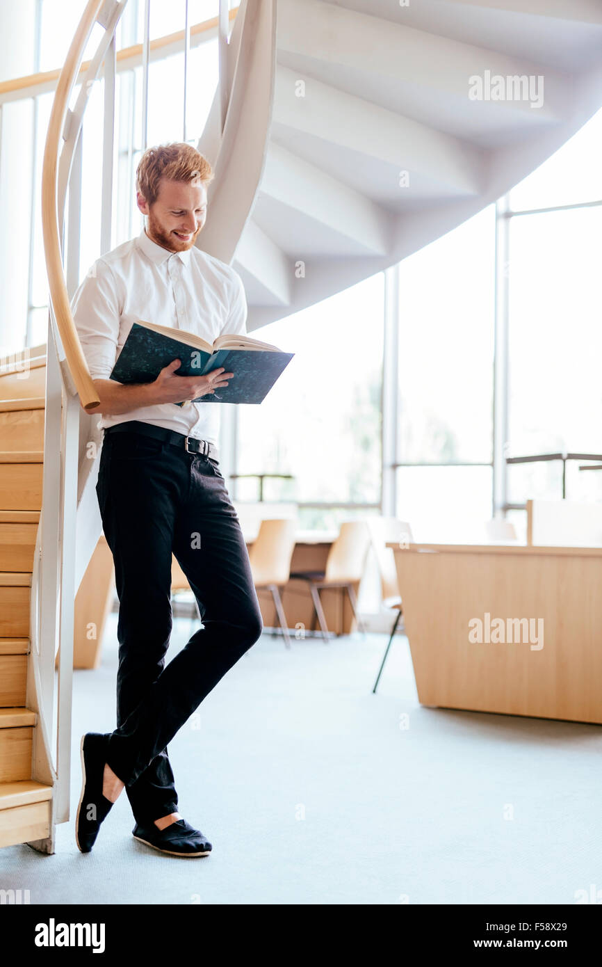 Handsome smart guy reading a book in a library Stock Photo - Alamy