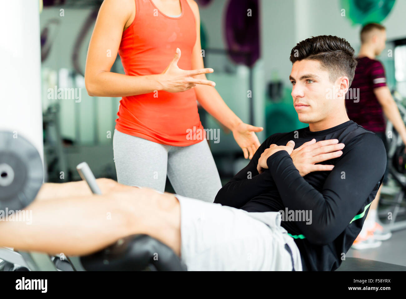 Beautiful young woman instructing a young man in the gym and ...