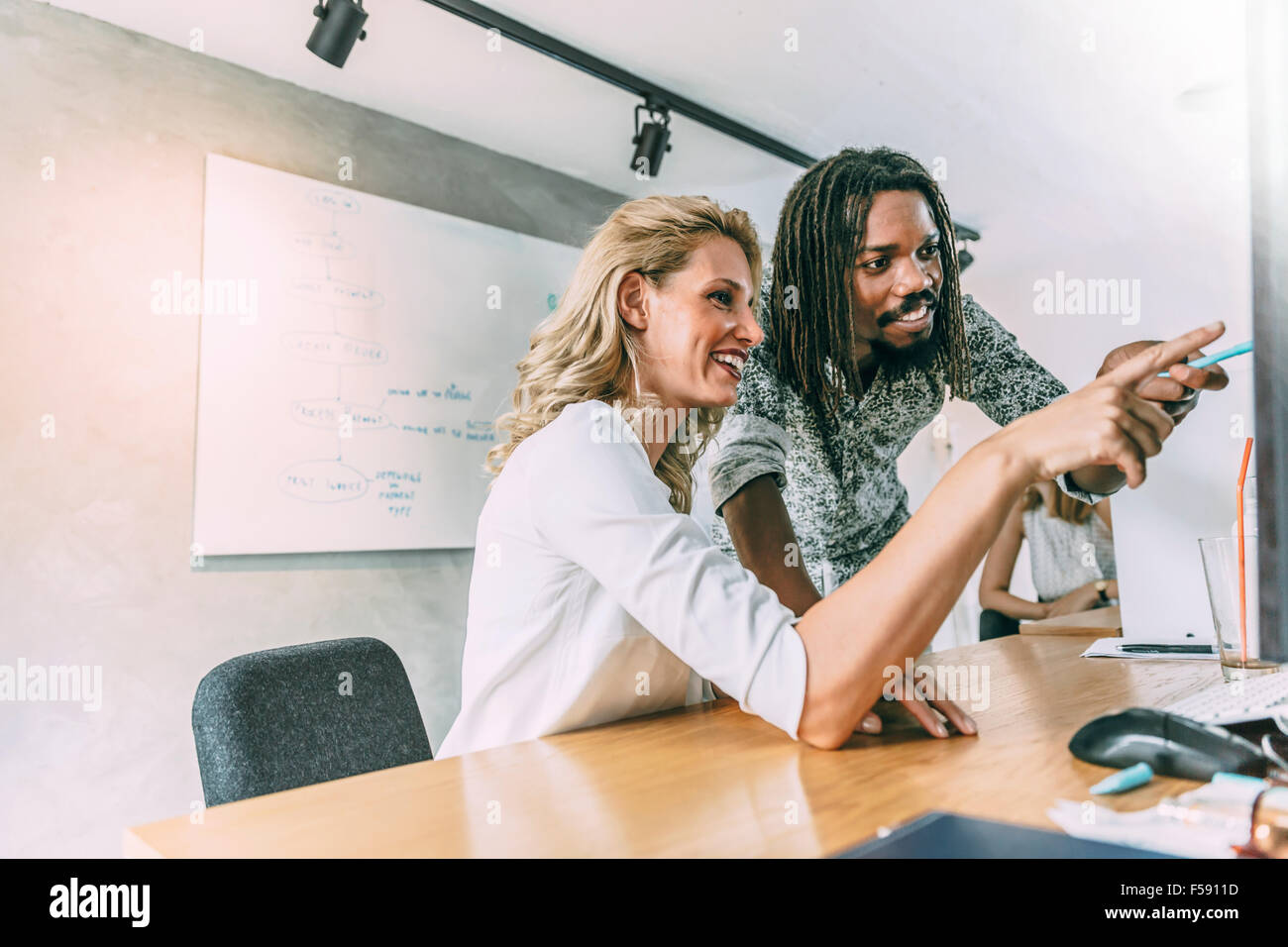 Coworkers in office pointing at desktop and discussing contents ...