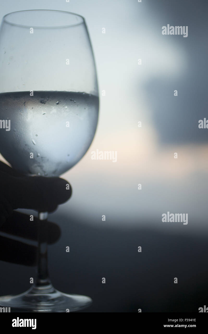 Water glass held in hand by man in silhouette with sky and clouds ...