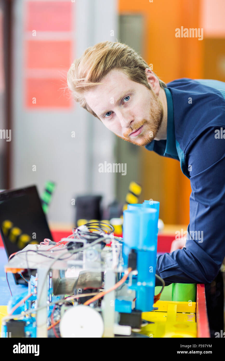 Male electrical engineer programming a robot during robotics class ...