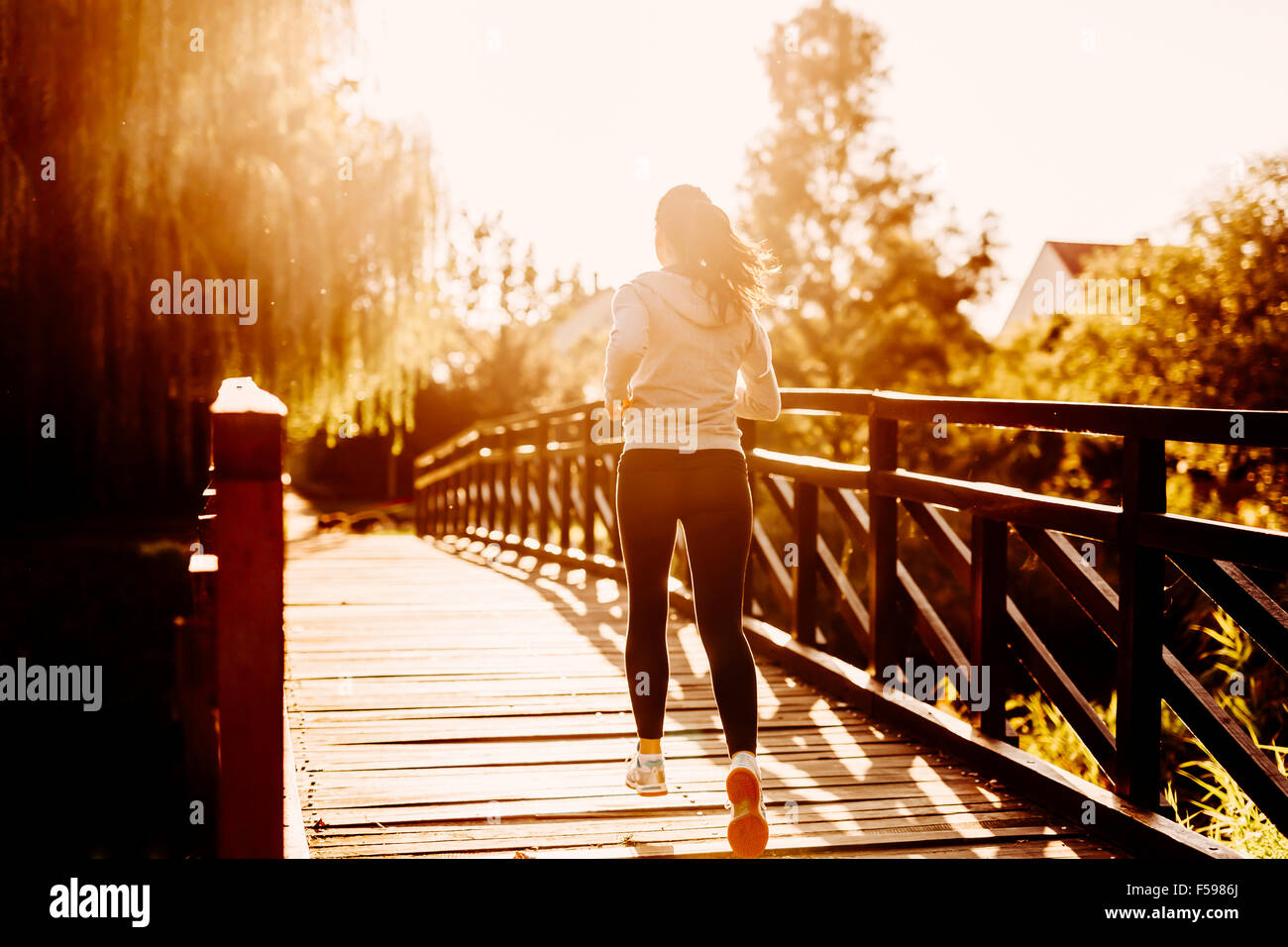 Beautiful female jogger running during sunset across bridge Stock Photo ...
