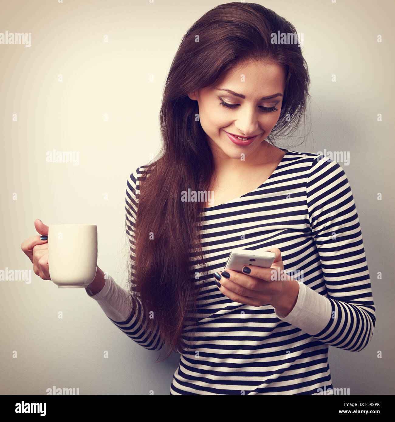 Cute smiling casual woman texting sms on mobile phone and drinking ...