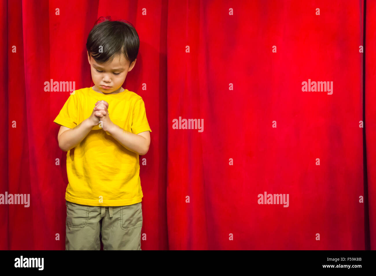 Mixed Race Boy with Praying Hands in Front of Red Curtain Stock Photo ...
