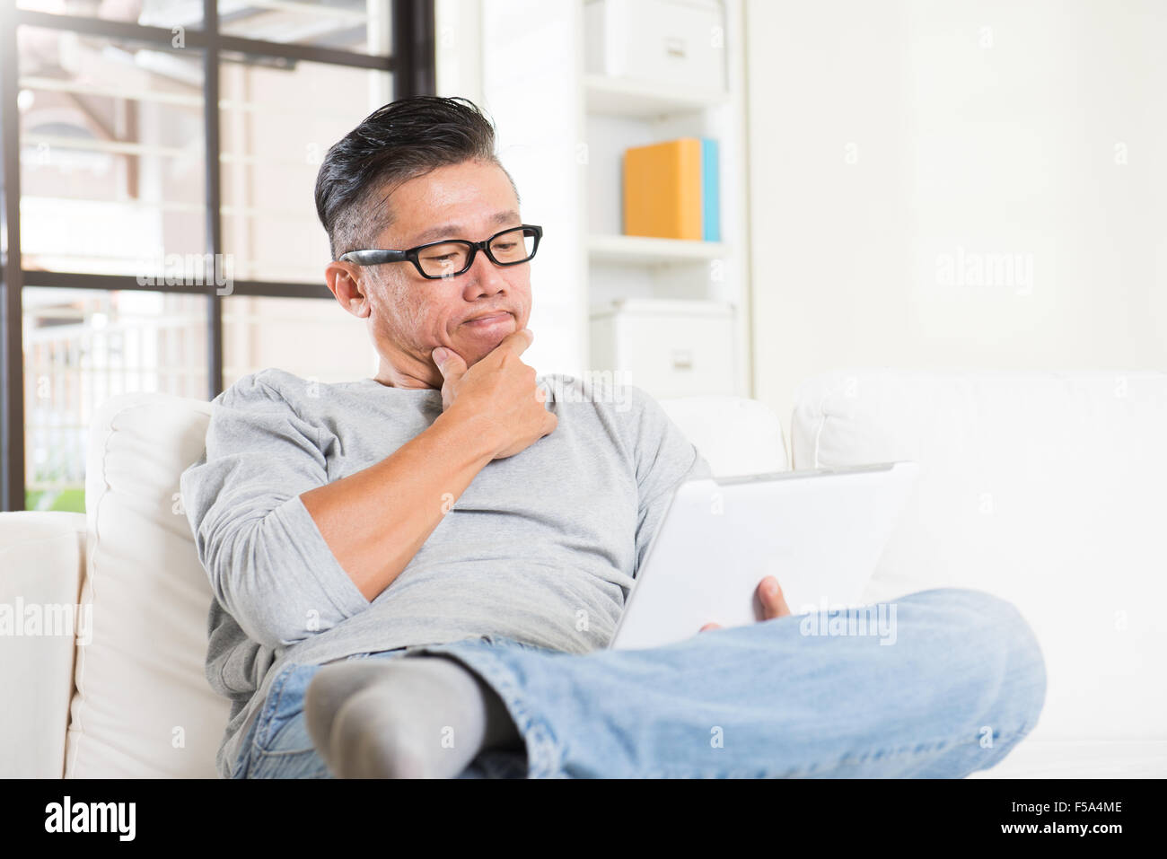 asian senior using tablet and thinking Stock Photo - Alamy