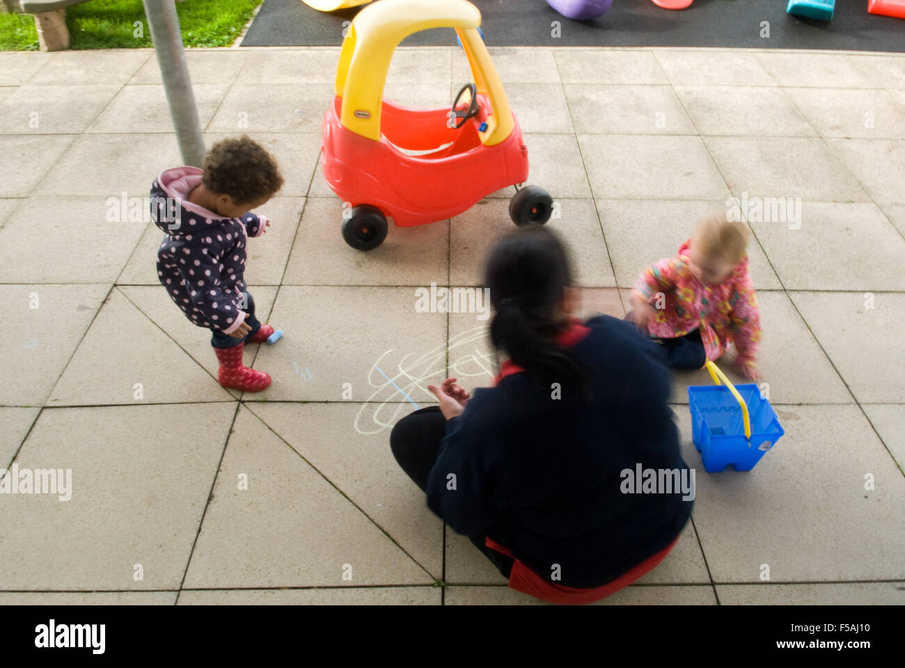 pre school teacher helping children to play outside Stock Photo - Alamy