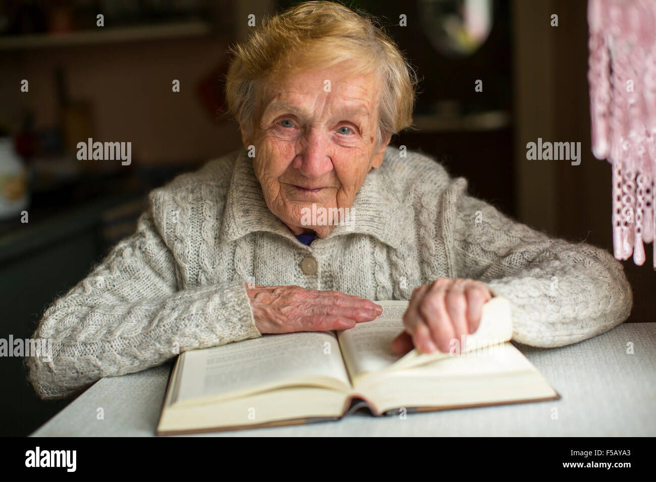 Old woman reading a book sitting at the table Stock Photo - Alamy