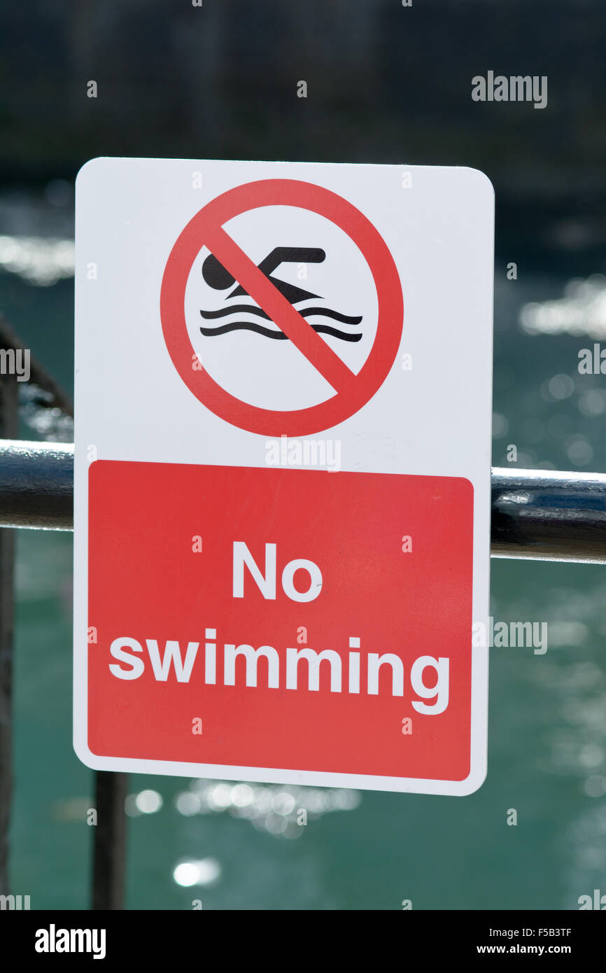 No Swimming sign on railings besides harbour where lots of boats are ...