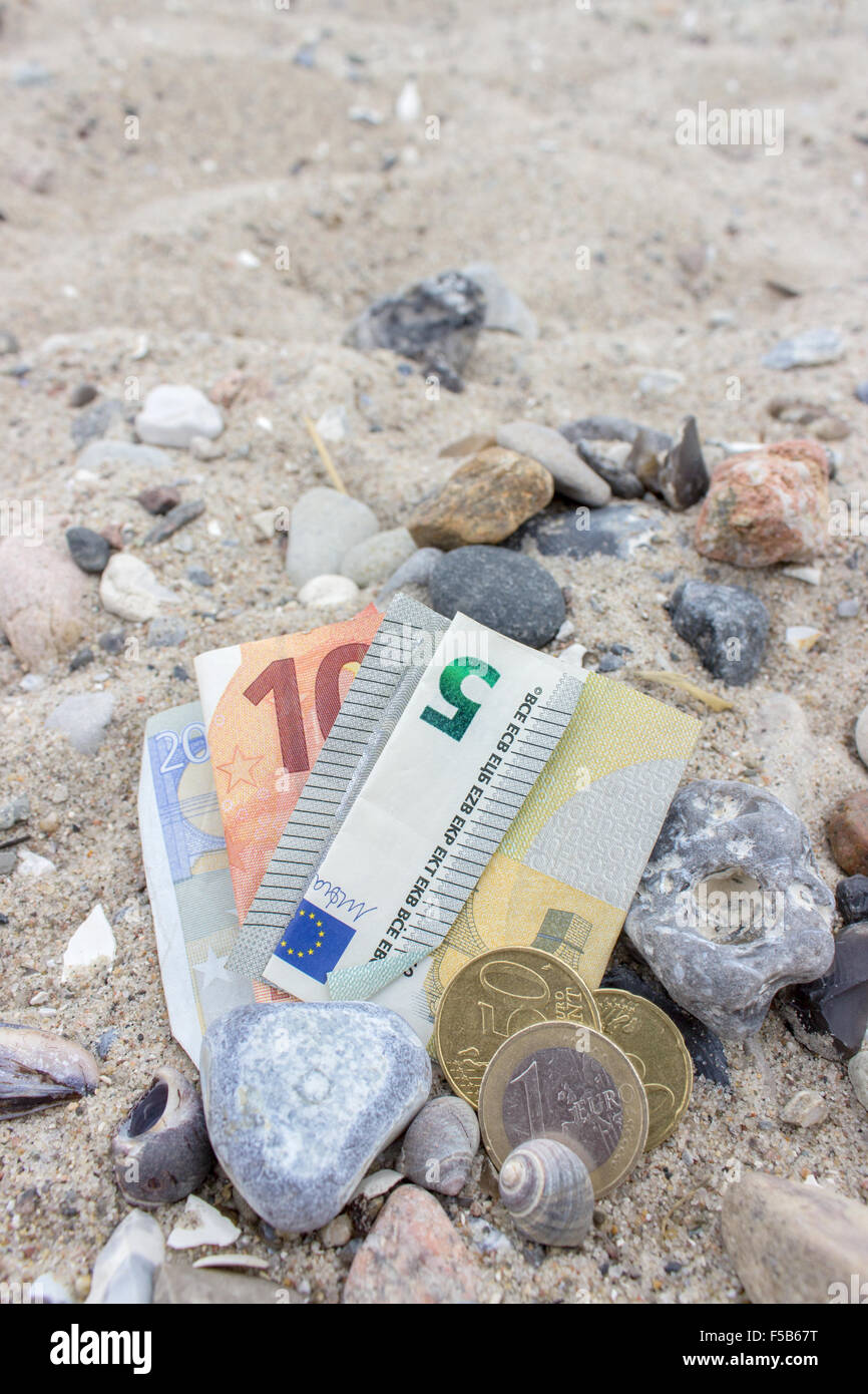Coins, Bills, stones and shells in the sand Stock Photo - Alamy
