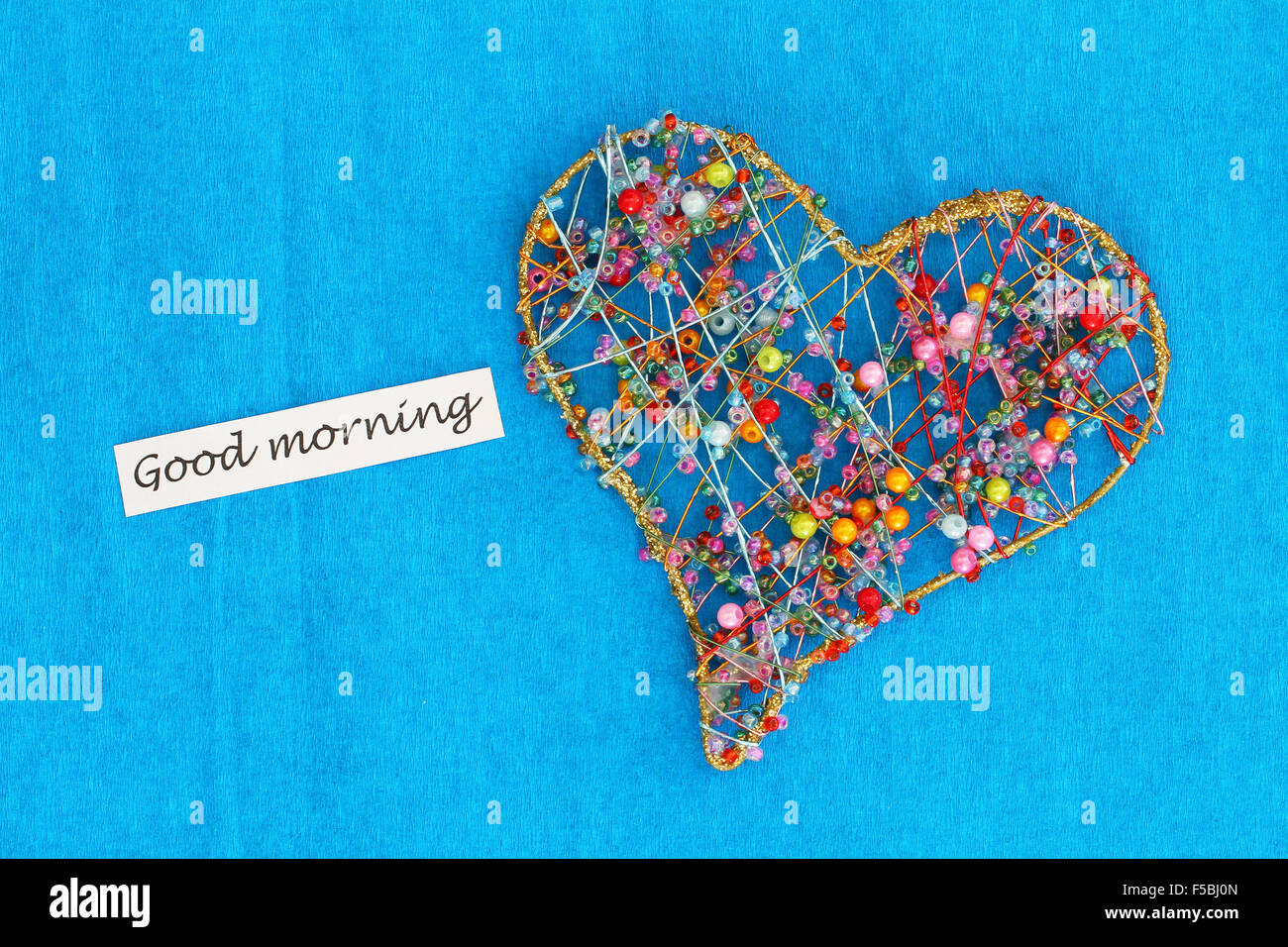 Good morning card with heart made of colorful beads on blue surface ...