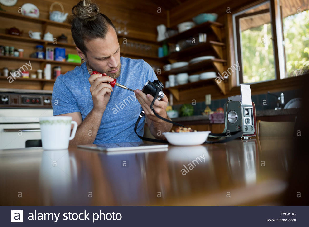 Man fixing retro camera at cabin kitchen table Stock Photo - Alamy