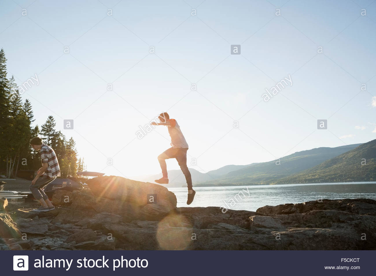 Young men jumping over rocks at sunny lakeside Stock Photo - Alamy