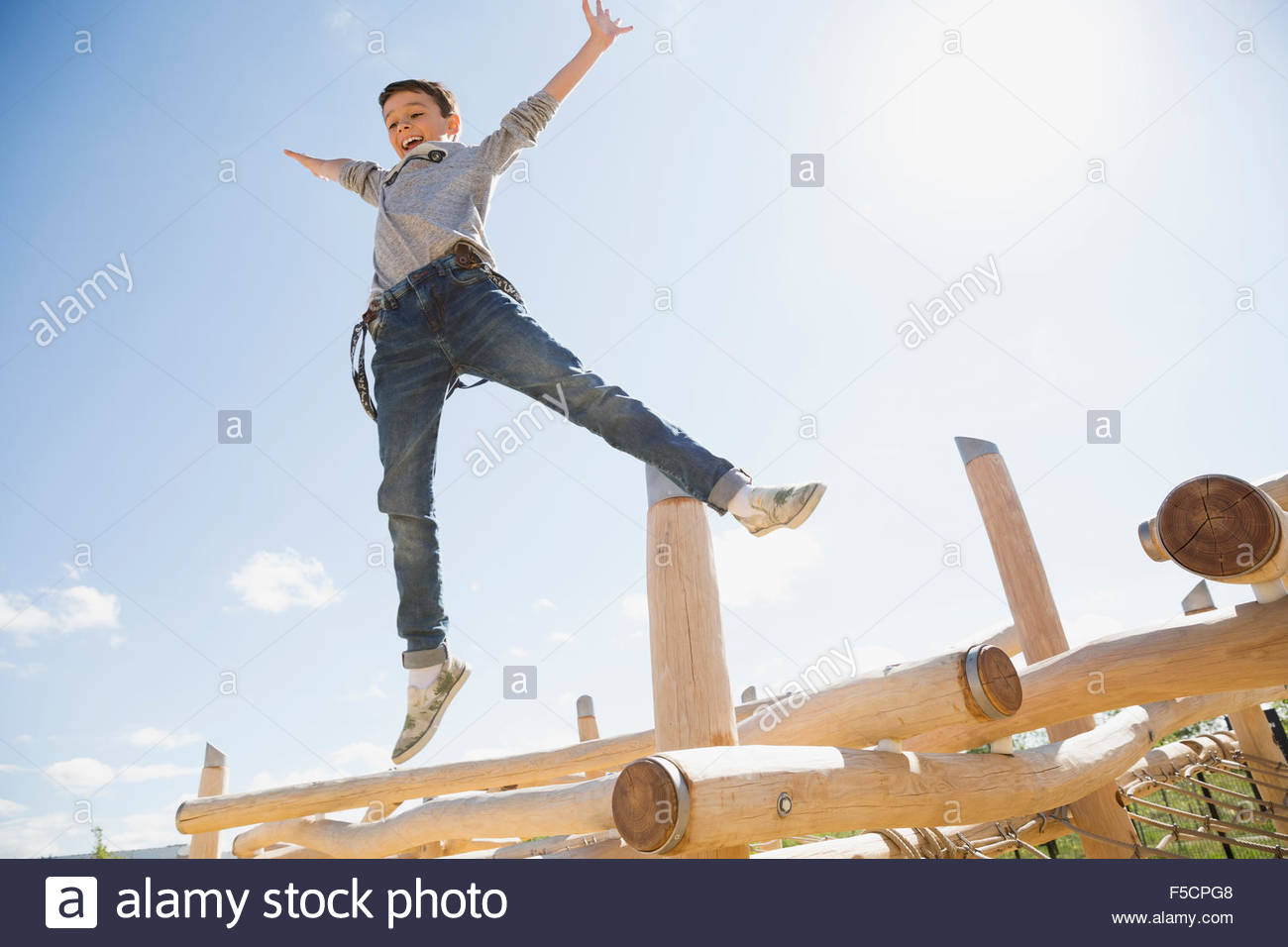 Carefree boy jumping off logs at sunny playground Stock Photo - Alamy