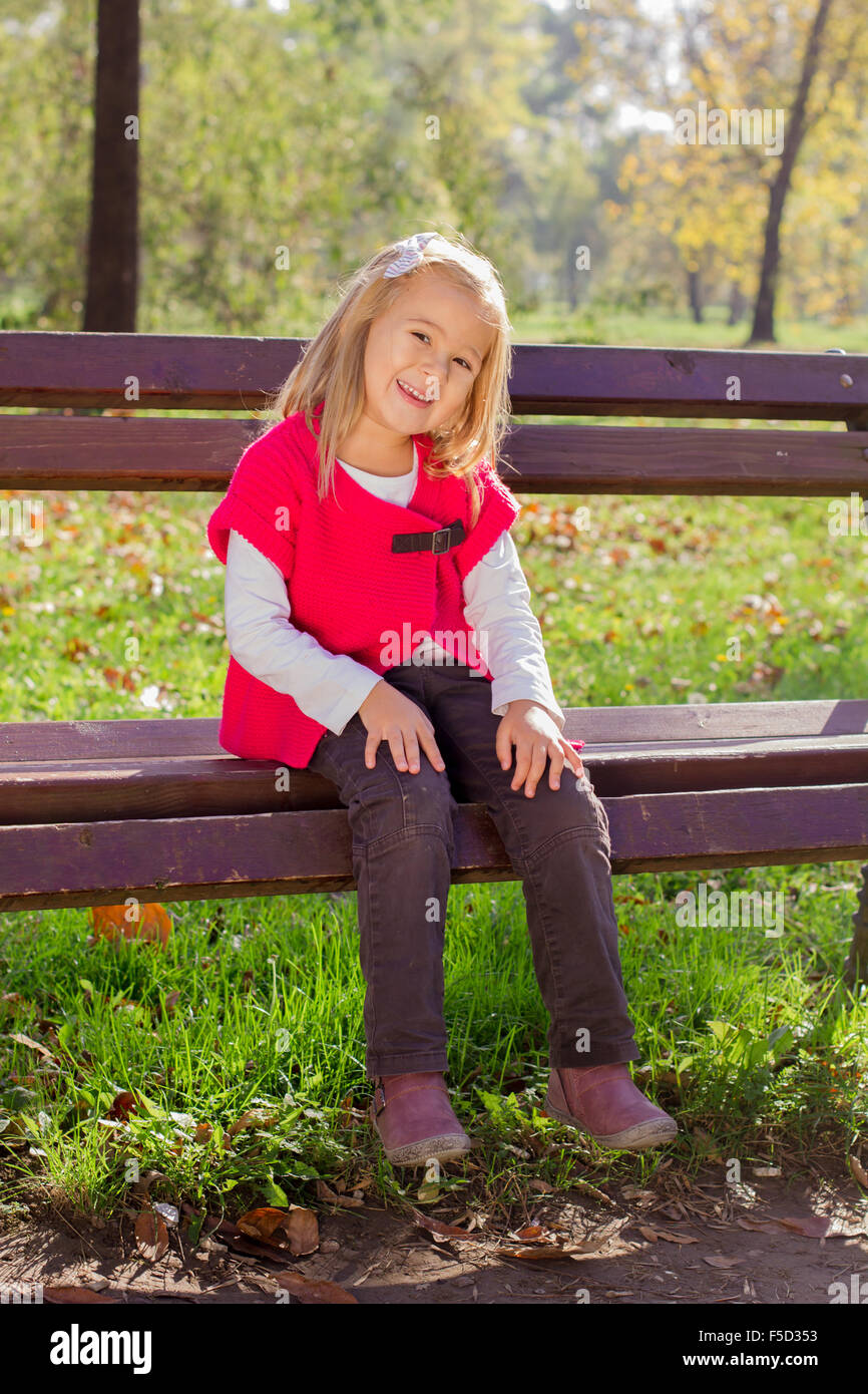 Happy little girl sitting on bench girl in the park. Autumn season ...