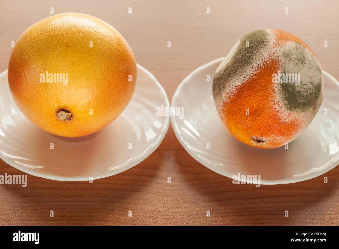 Ripe and moldy grapefriut on plate at wooden table. Difference between ...