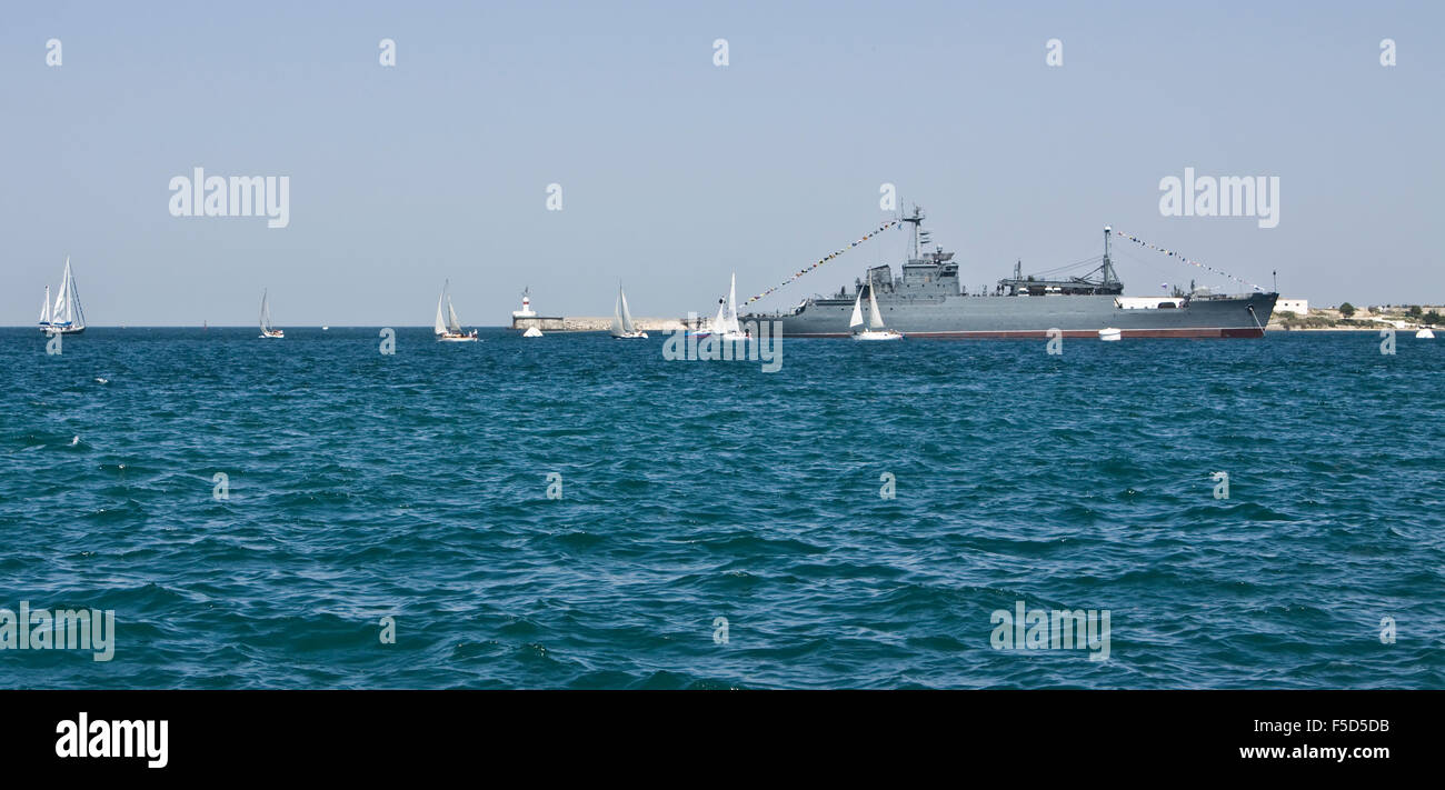 Big military ship and many little white sailing boats around in sea ...
