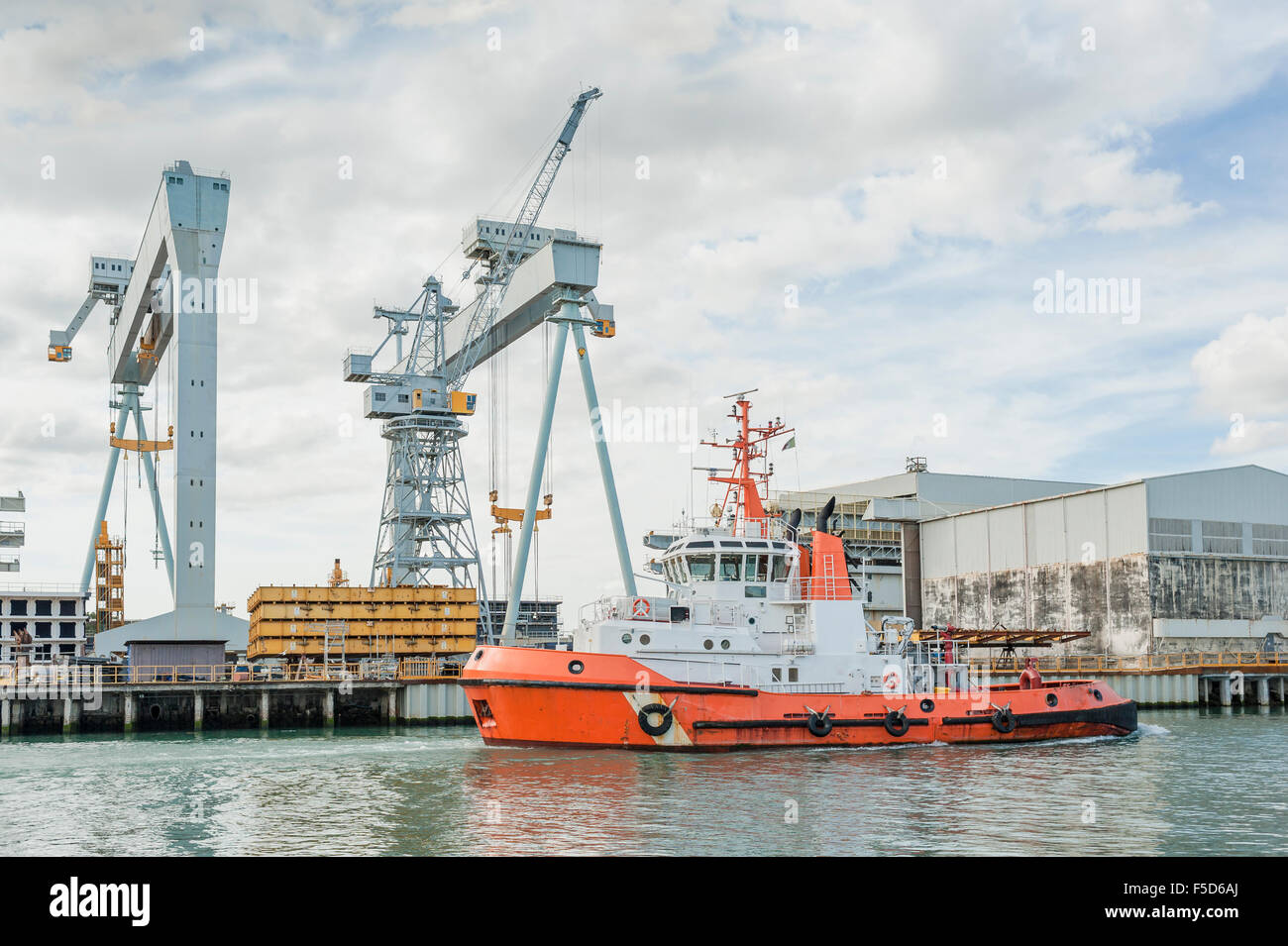 Tugboat at work at a shipyard with cranes in the background Stock Photo ...