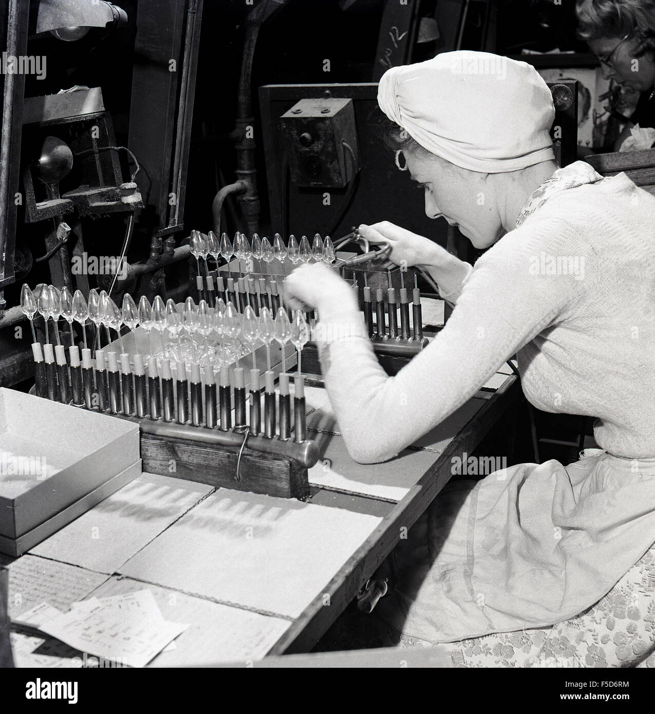 1950s historical, female factory worker at work assembling glass light ...