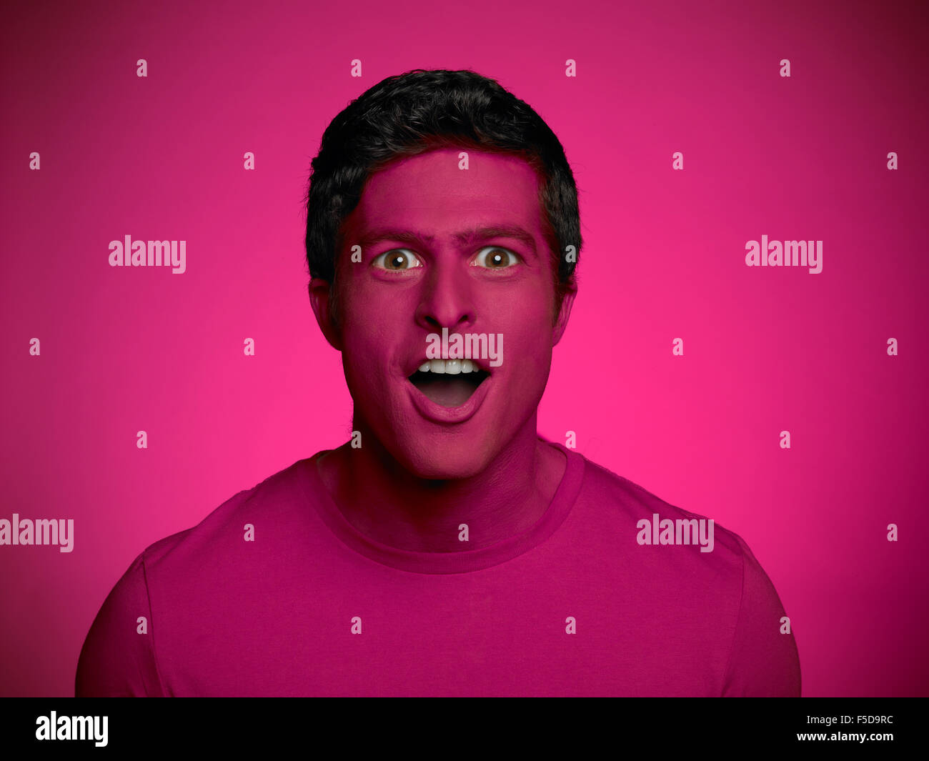 Happy and surprised young man with extra big eyes filtered on magenta ...