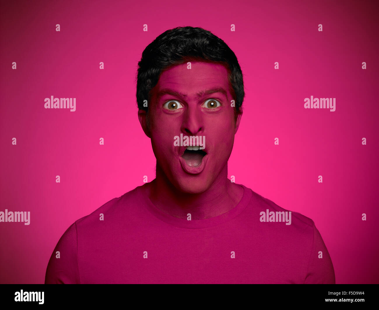 Happy and surprised young man with extra big eyes filtered on magenta ...