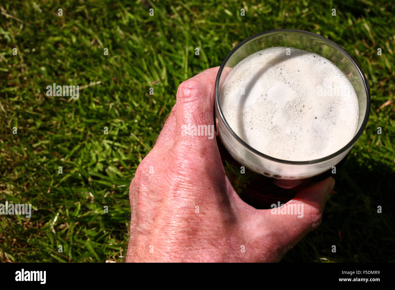 Mans hand holding a pint glass of bitter beer outside in the summer ...