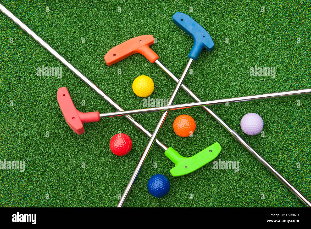Assorted miniature golf putters and balls askew on synthetic grass ...