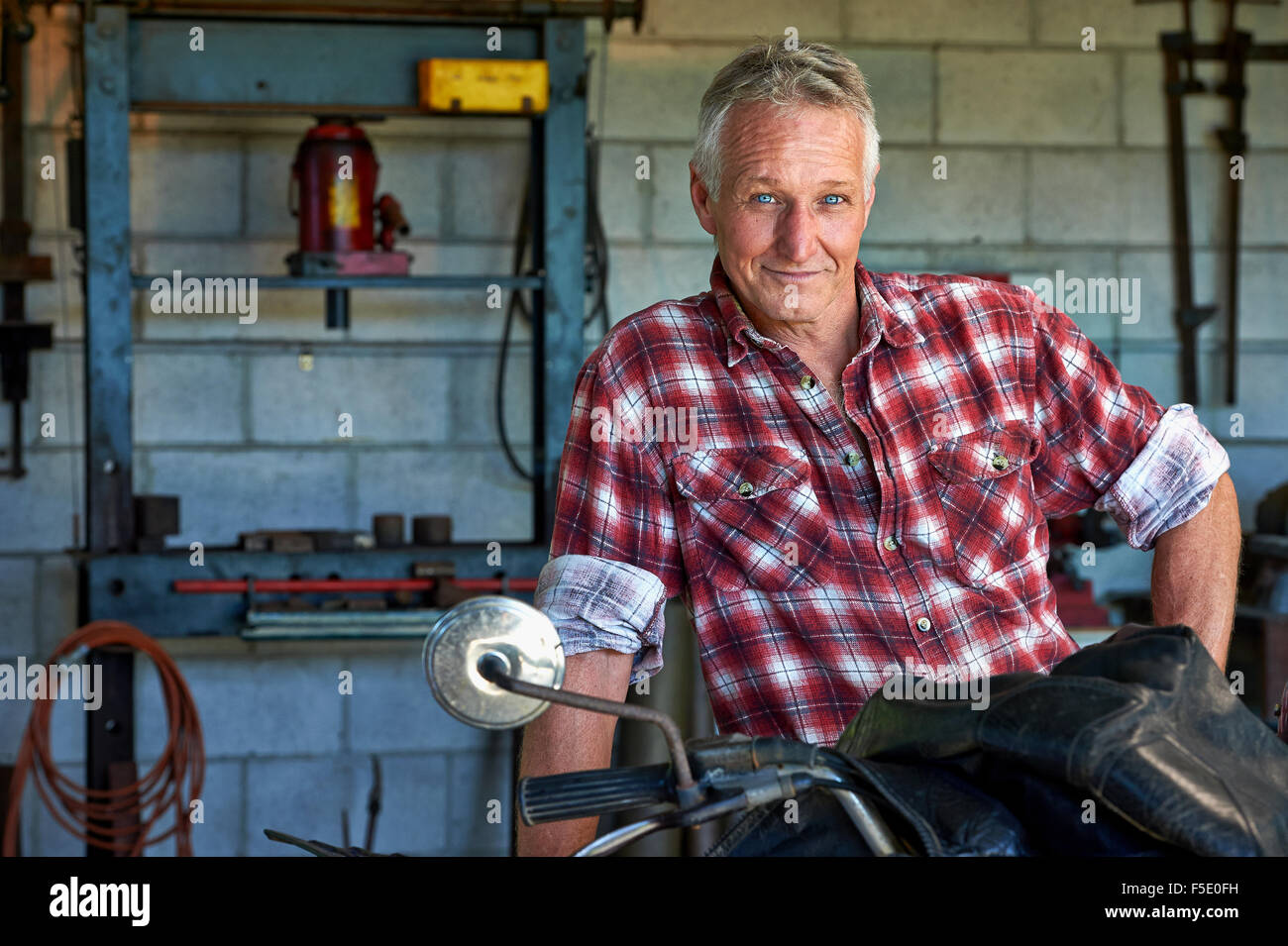 Middle aged man next to his old motor bike. His tough exterior is ...