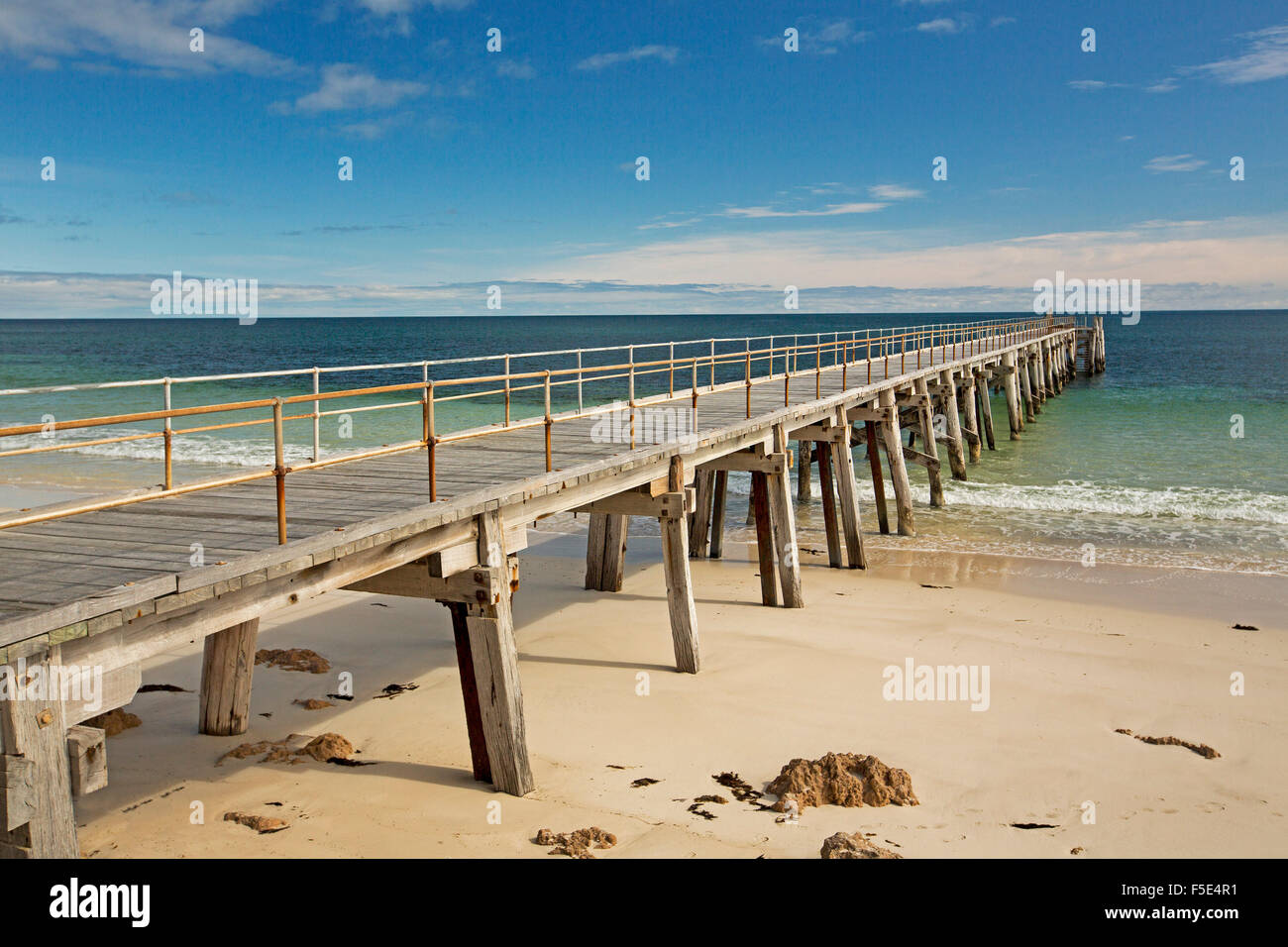 Long wooden jetty spearing out from sandy beach to blue waters of ocean ...