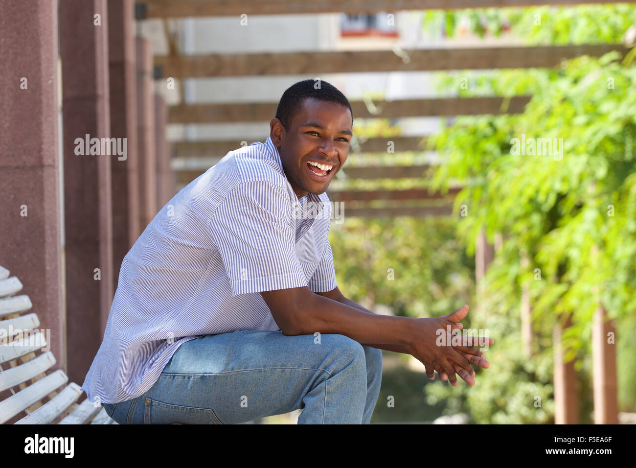 Side portrait of a young black man sitting outside laughing Stock Photo ...