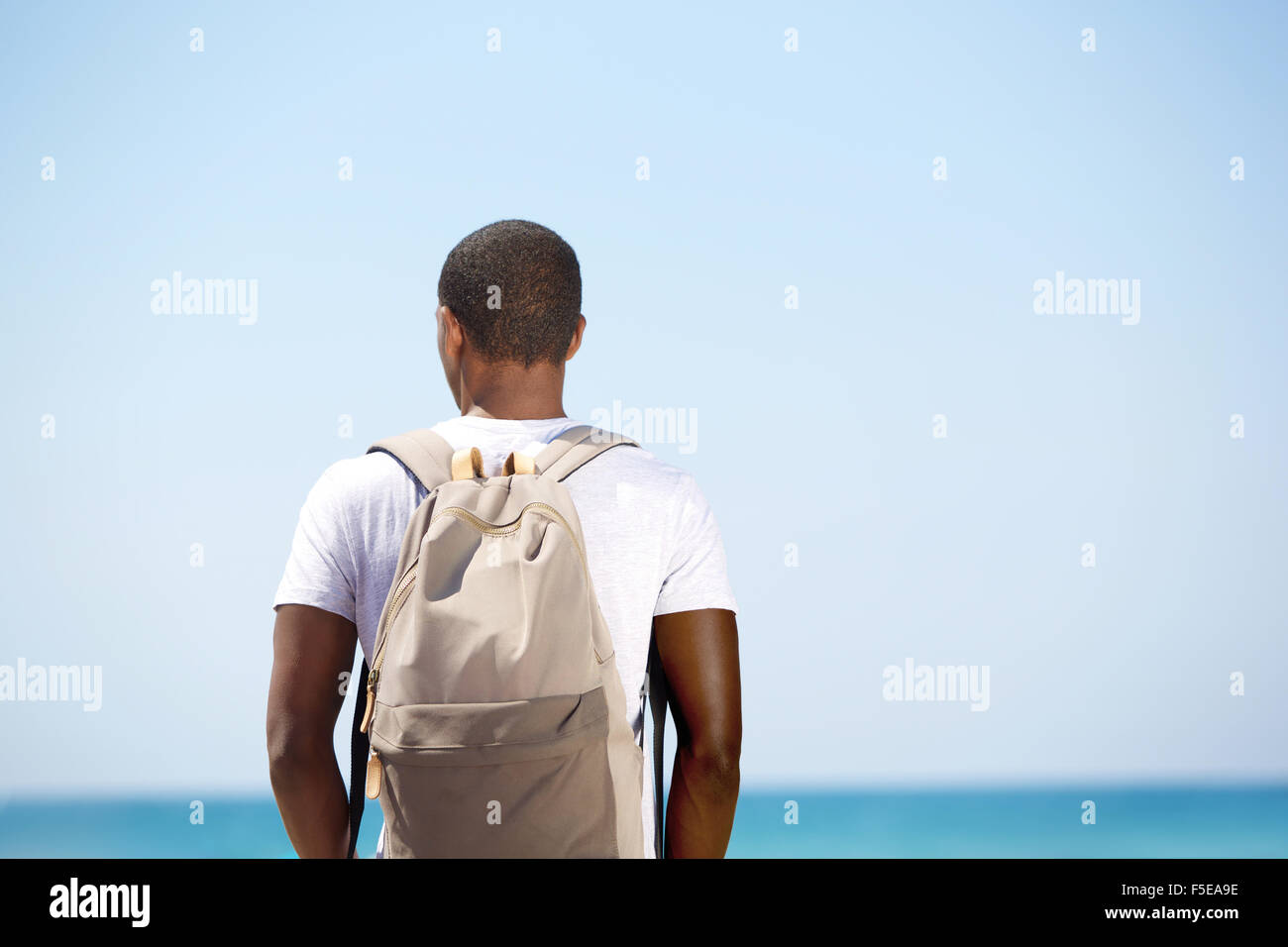 Rear portrait of a black man standing with backpack by the sea Stock ...