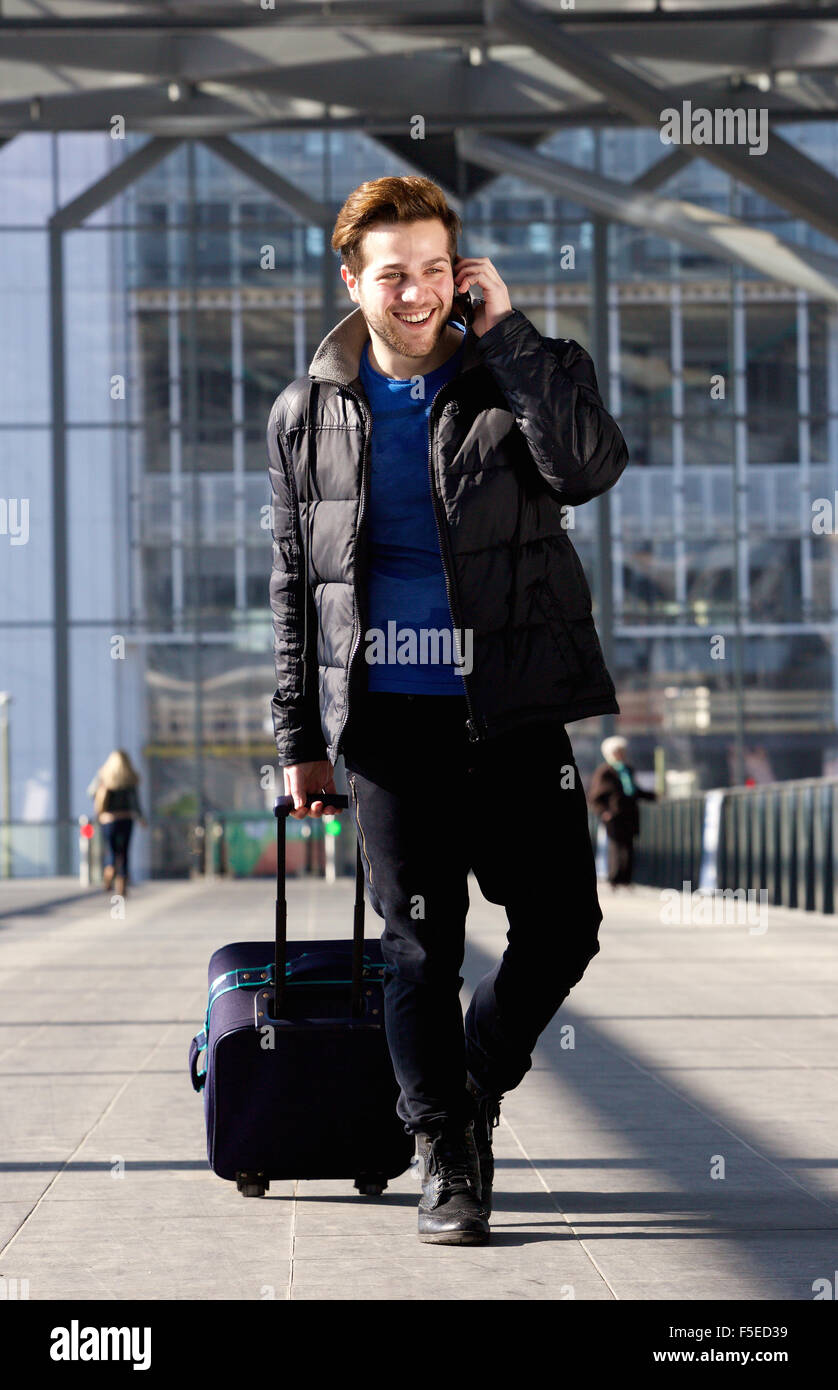 Portrait of a cool guy walking with mobile phone and bag at station ...
