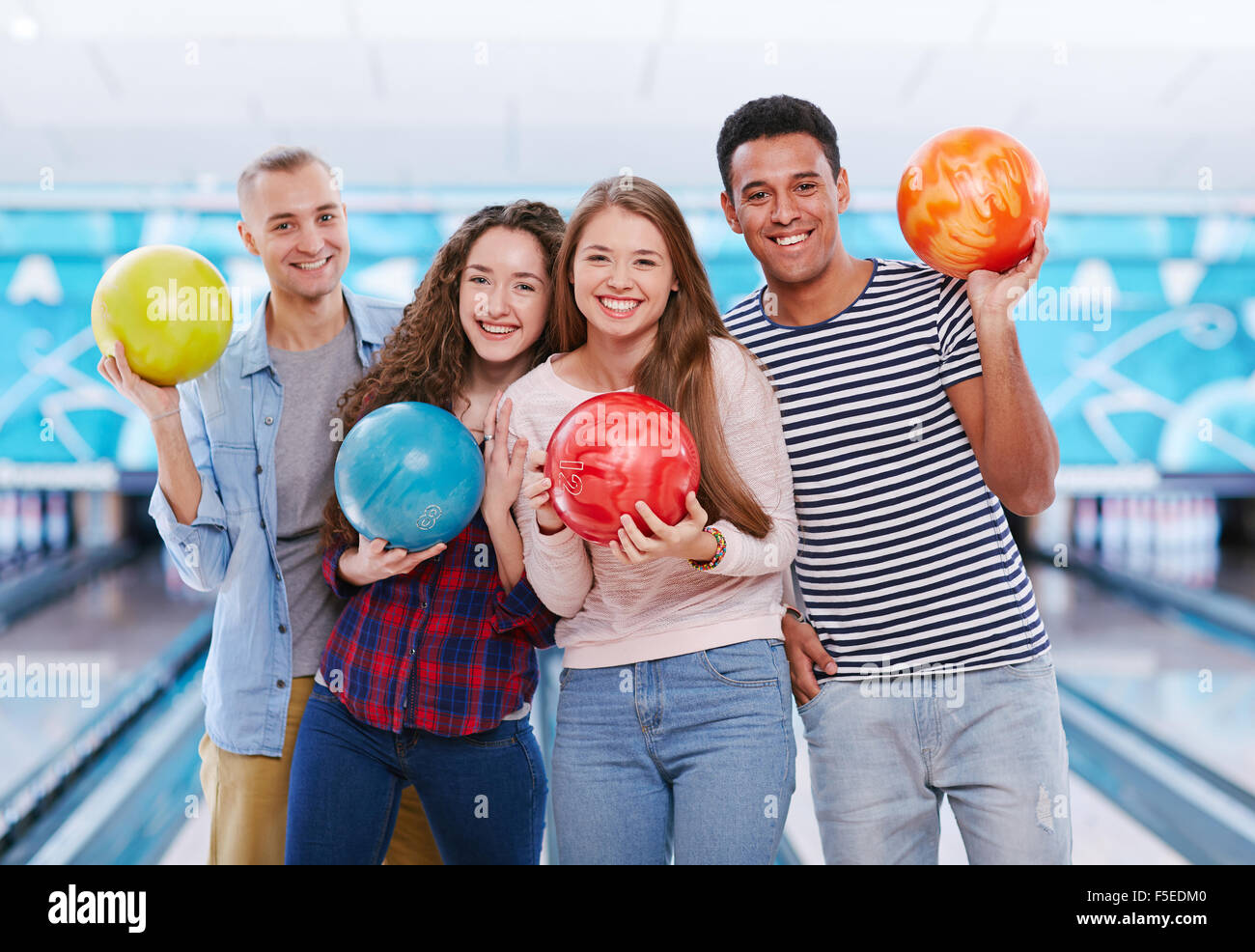 Group of joyful young friends with bowling balls looking at camera ...