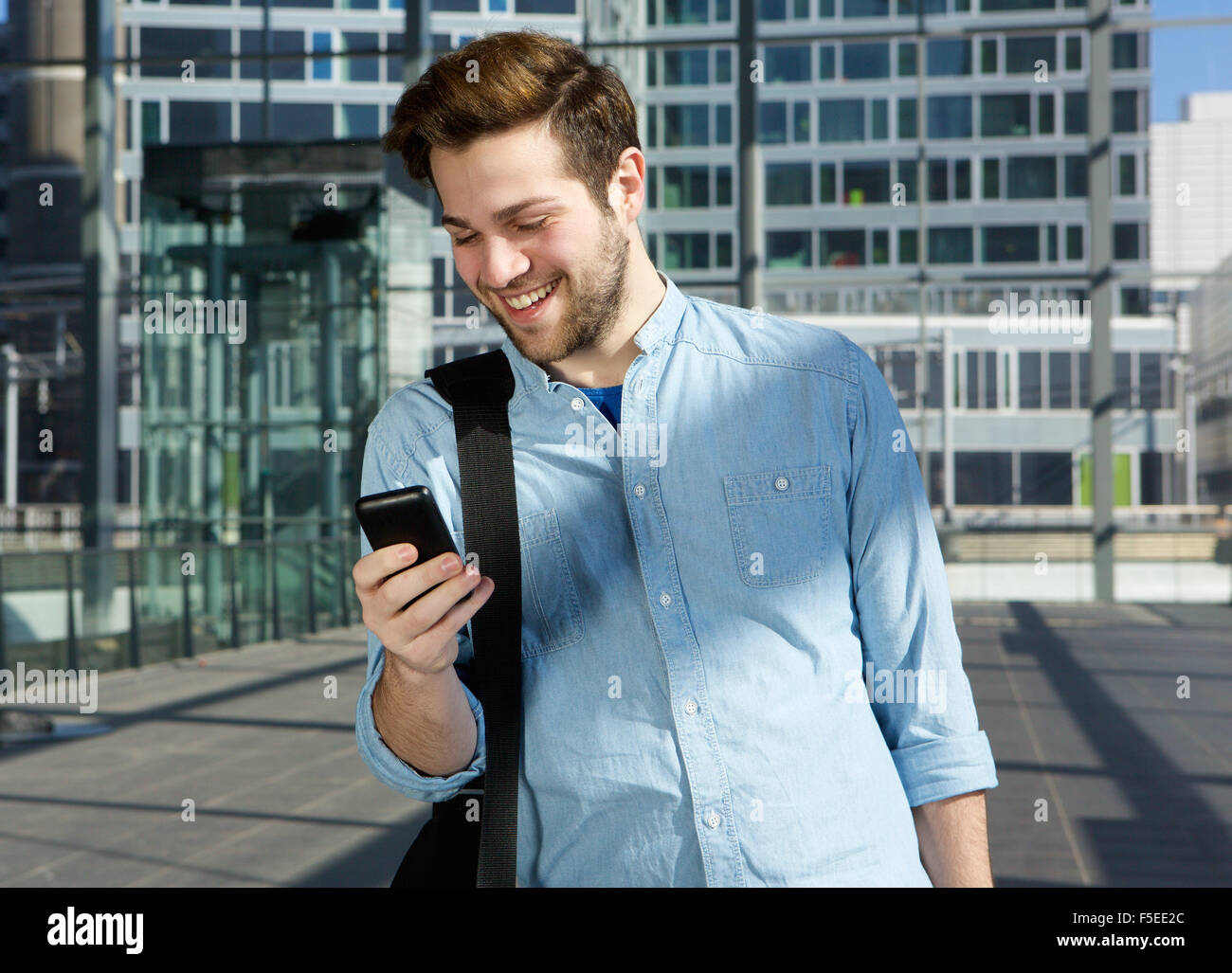 Portrait of a happy young man sending text message from mobile phone at ...