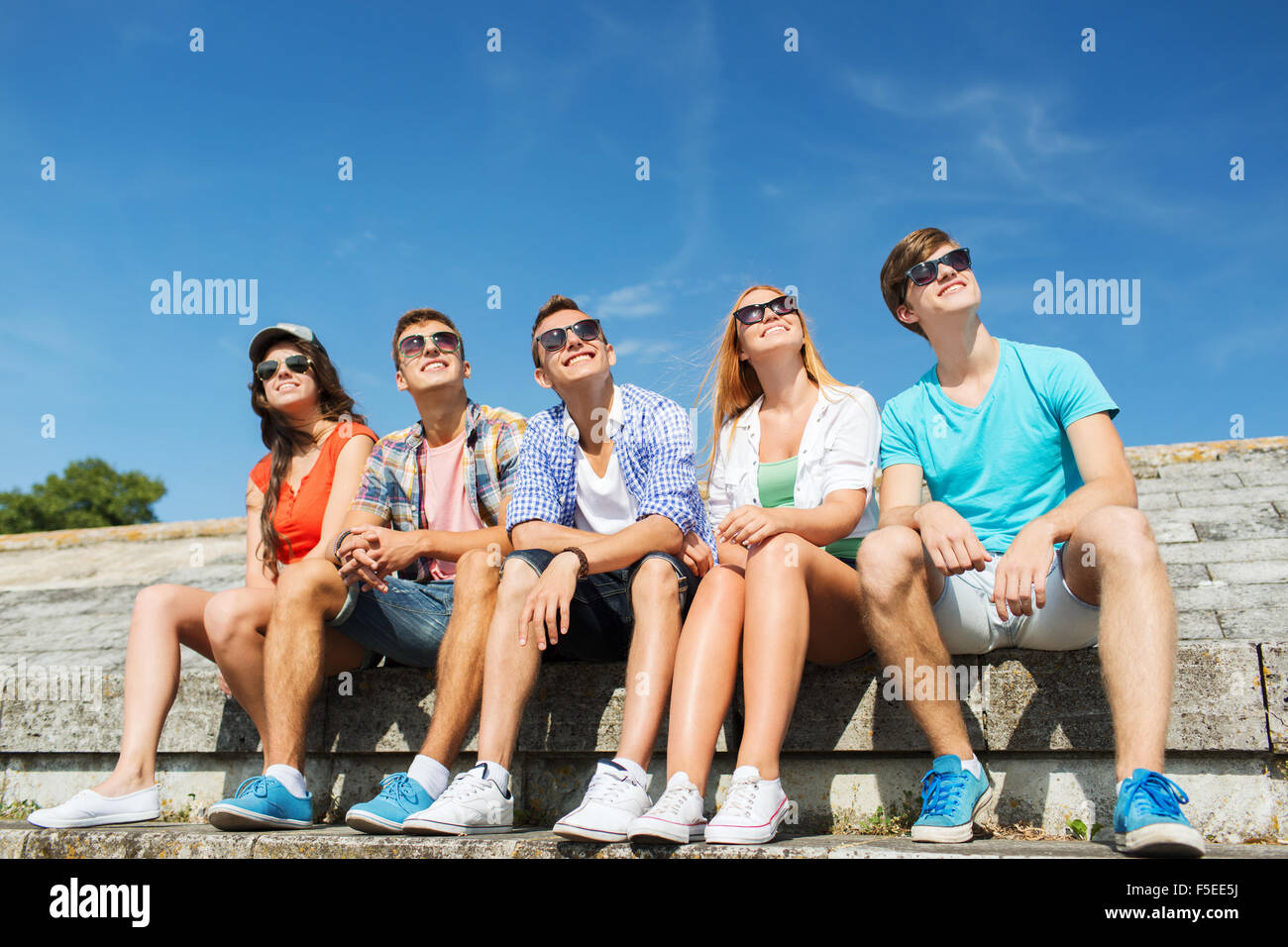 group of smiling friends sitting on city street Stock Photo - Alamy