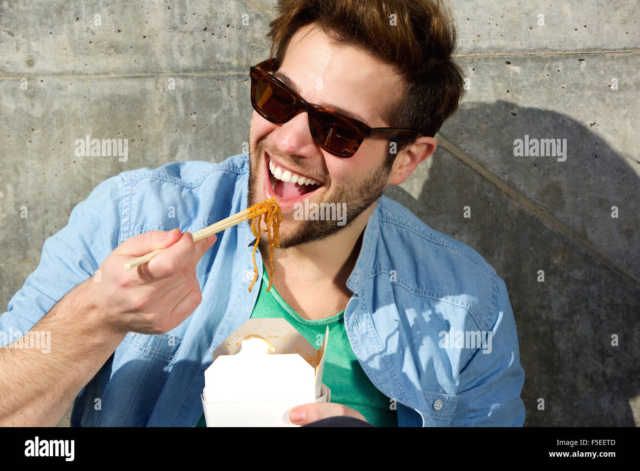 Close up portrait of a happy cool man eating chinese takeaway with ...
