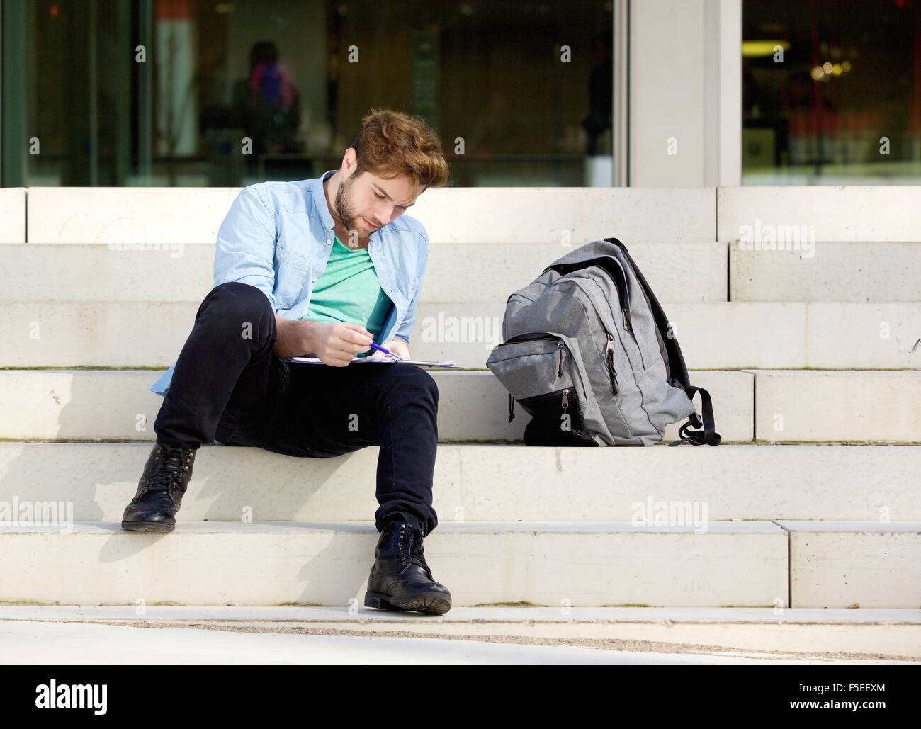 Portrait of a male student sitting outside on campus reading notes ...
