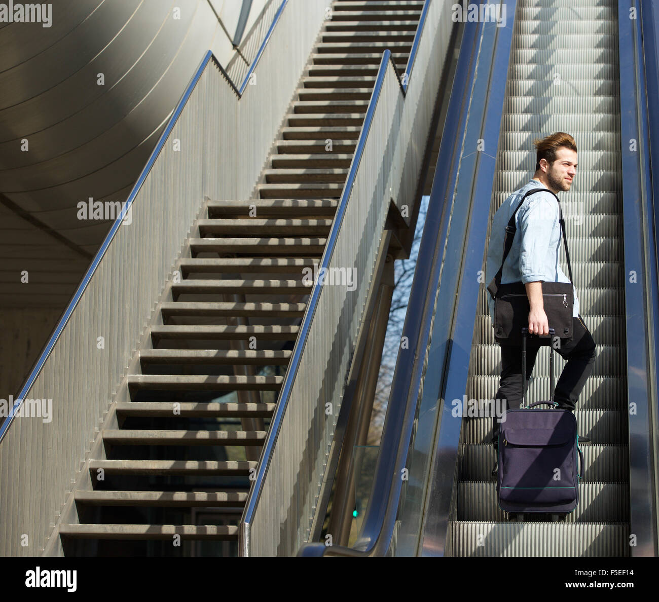 Portrait of a handsome man walking up escalator with travel bags Stock ...