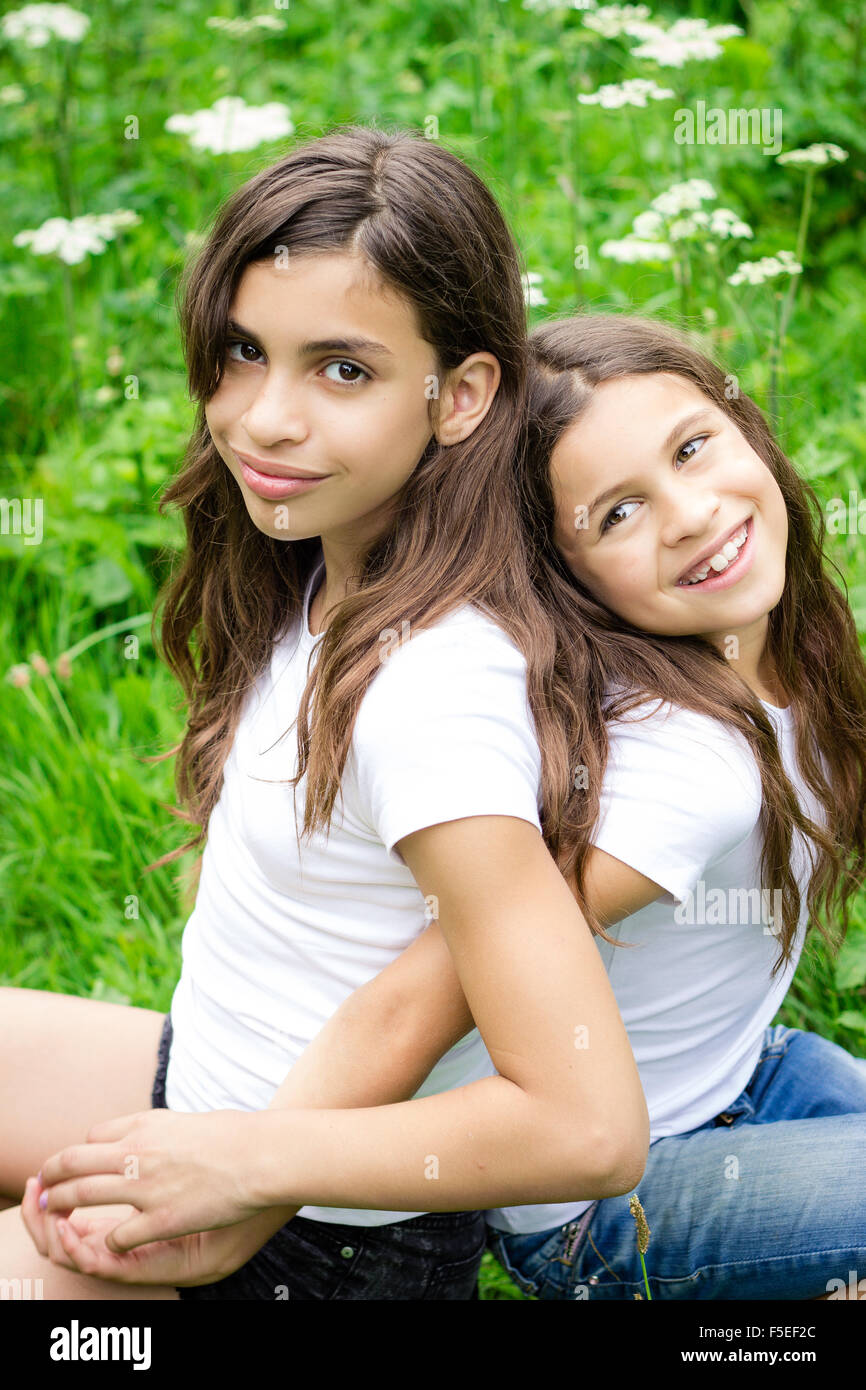 Portrait of two girls sitting back to back Stock Photo - Alamy