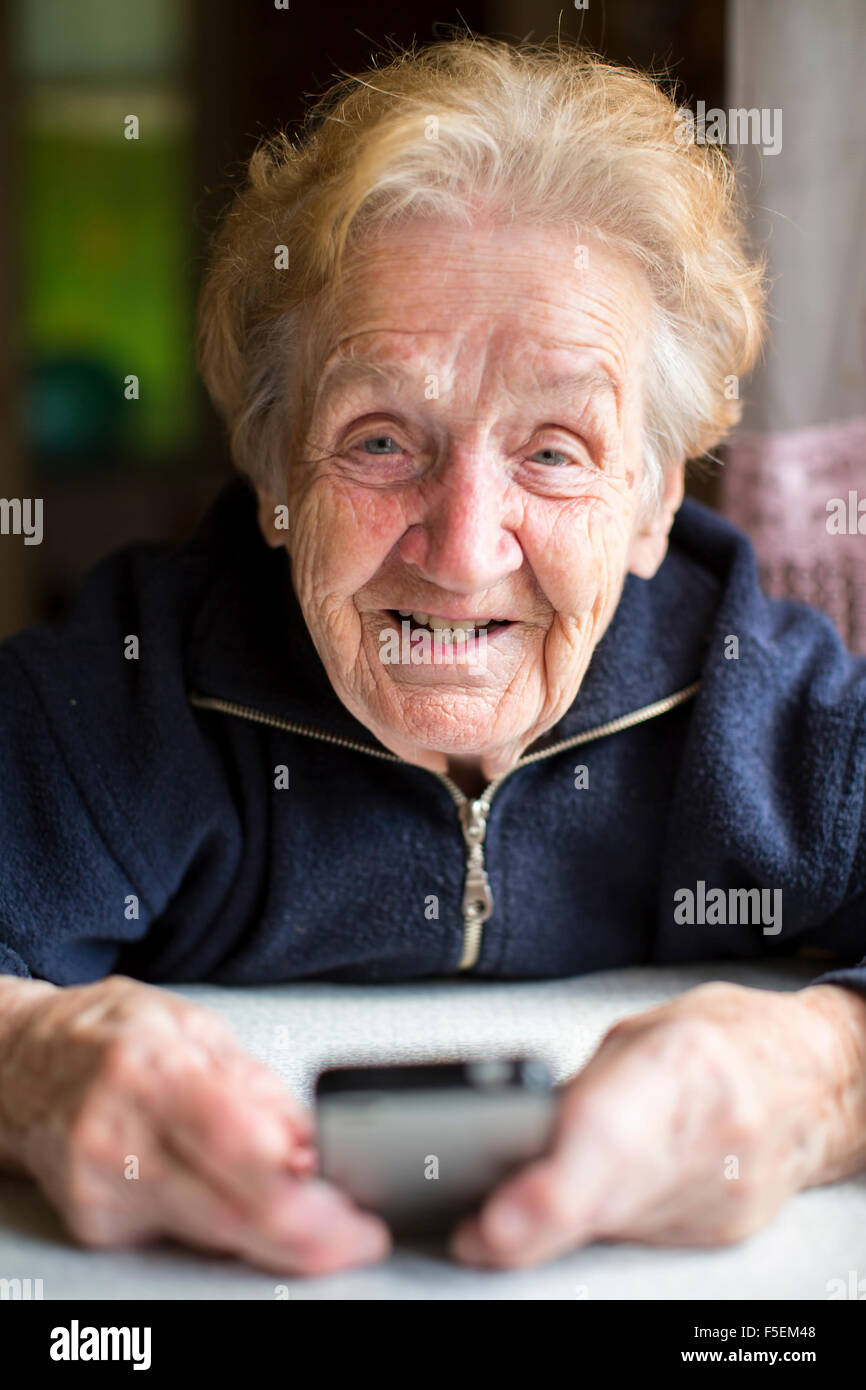 Old woman is typing on phone sitting on the table Stock Photo - Alamy