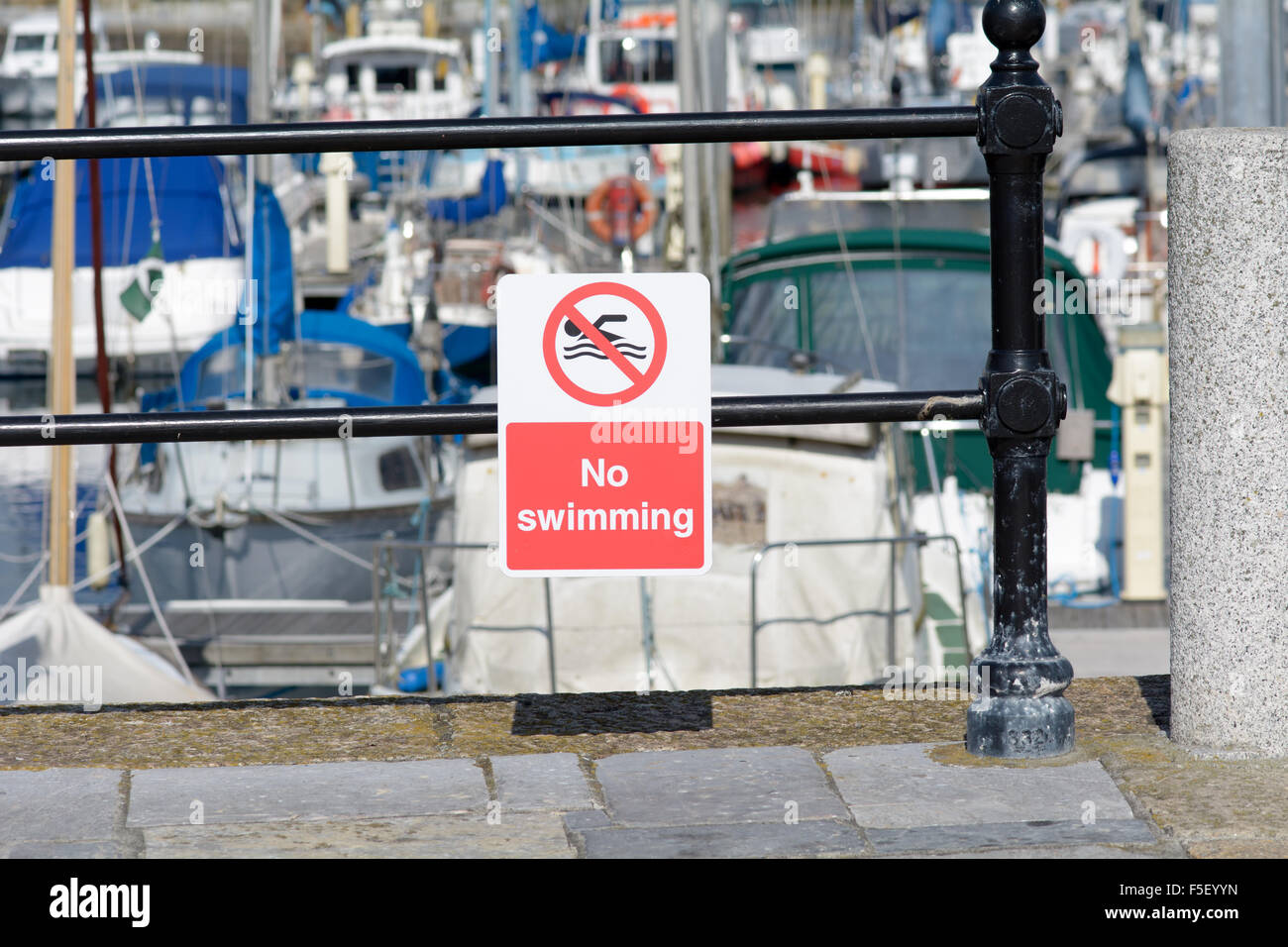 No Swimming sign on railings besides harbour Stock Photo - Alamy