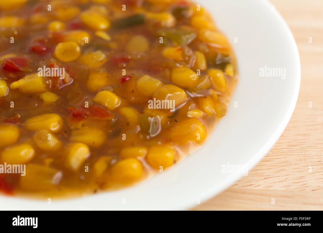 A white dish with corn relish on a wood table top illuminated with ...