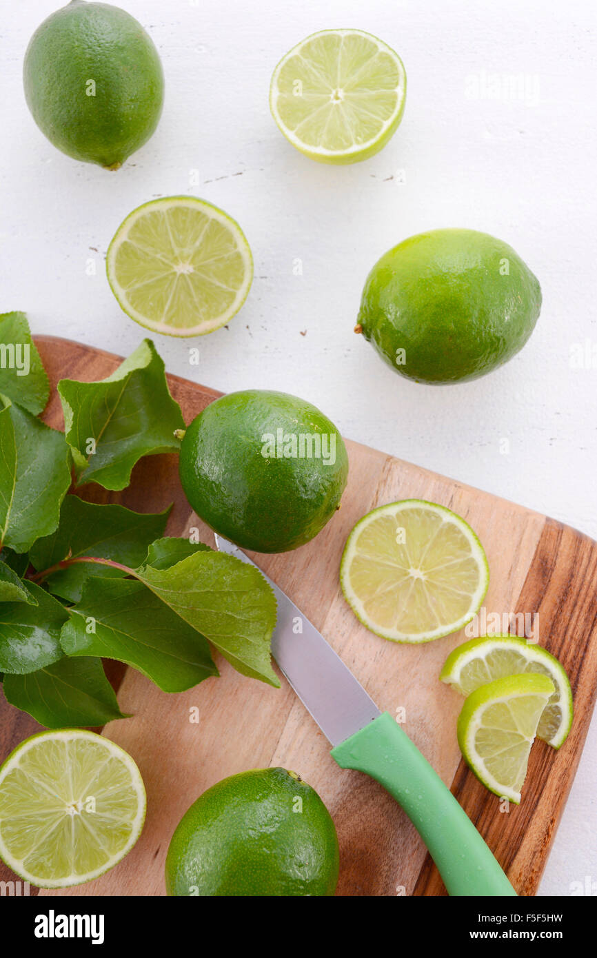 Whole and sliced limes on rustic white wood table with wooden chopping ...