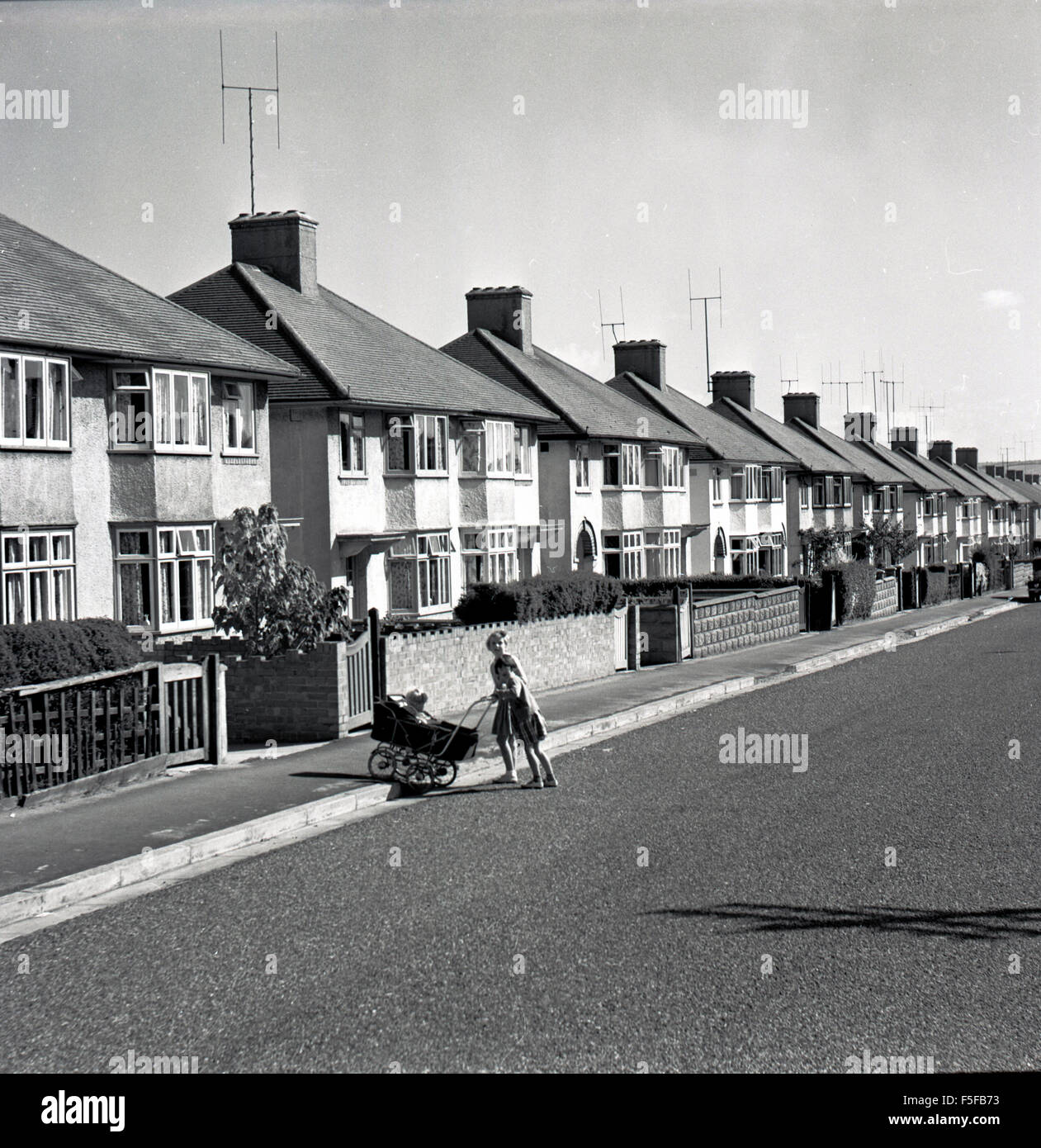 1950s historical, lady, child and pram cross a deserted street at ...