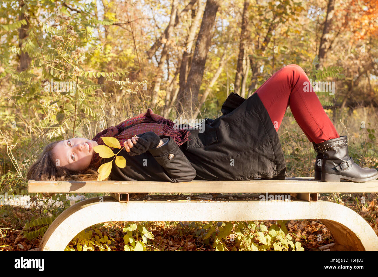 Beautiful girl lying on the bench and holding autumn leaf in a park ...