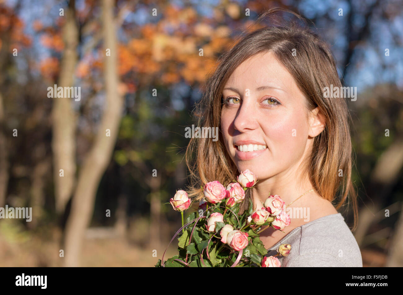 Portrait of a happy brunette girl holding miniature roses in the forest ...